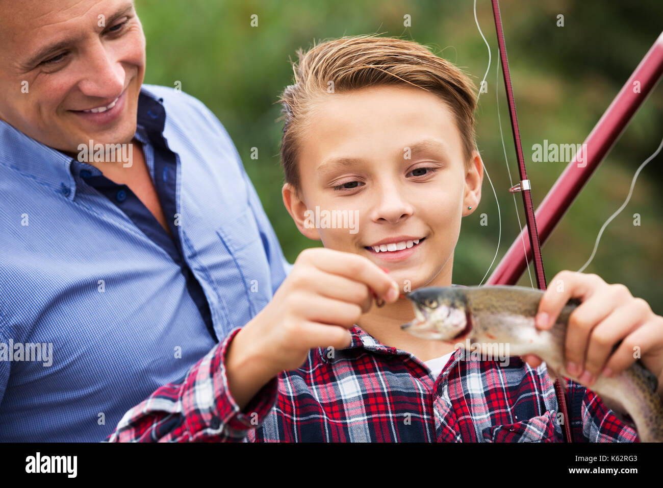 Happy teenage boy and his father holding taken freshwater fish in hands ...
