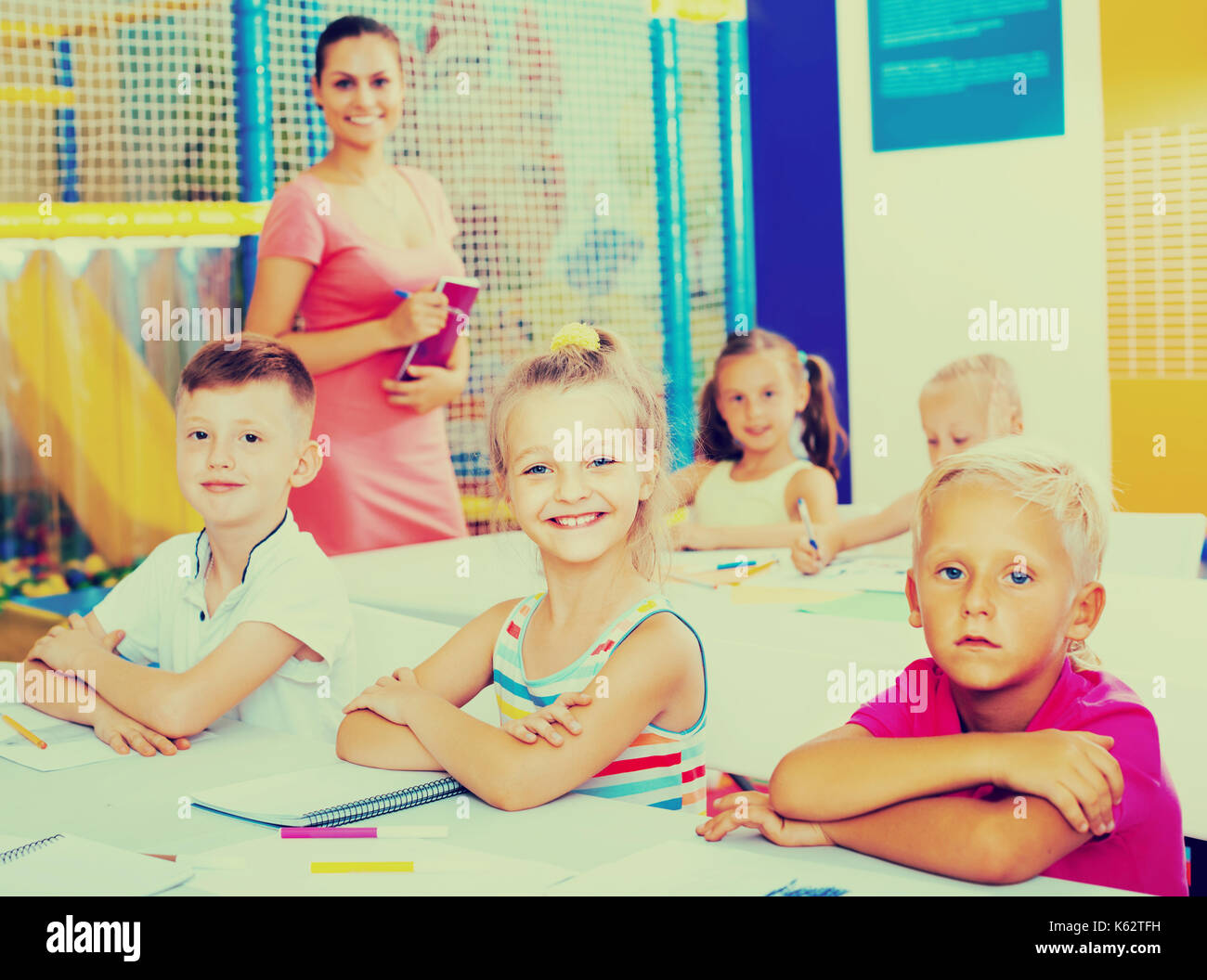 joyful smiling primary school kids sitting at school desks at lesson ...