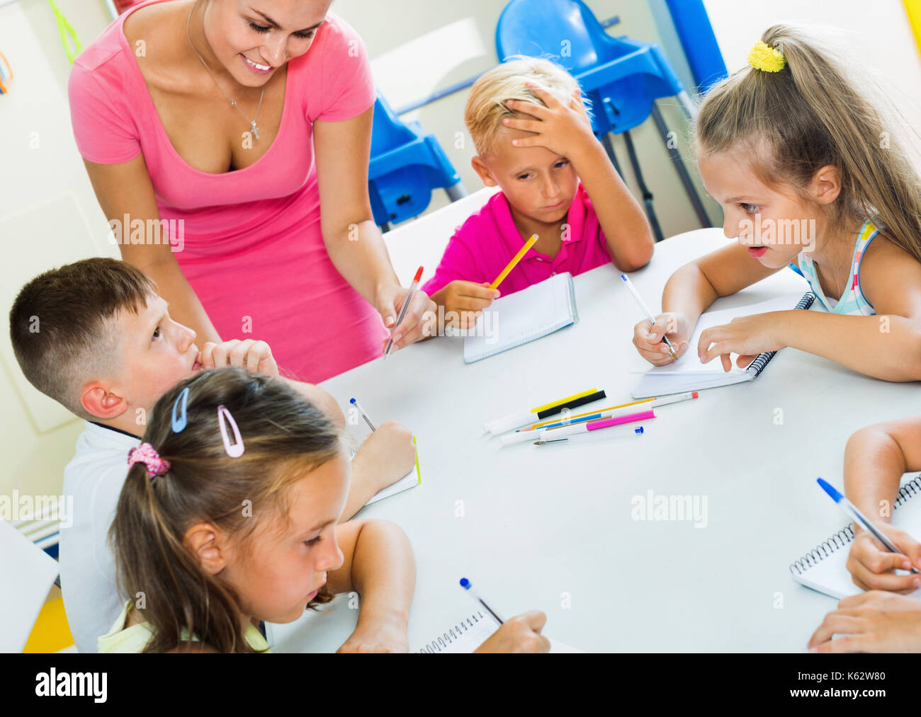 Happy smiling diligent kids writing together with tutor at school class ...