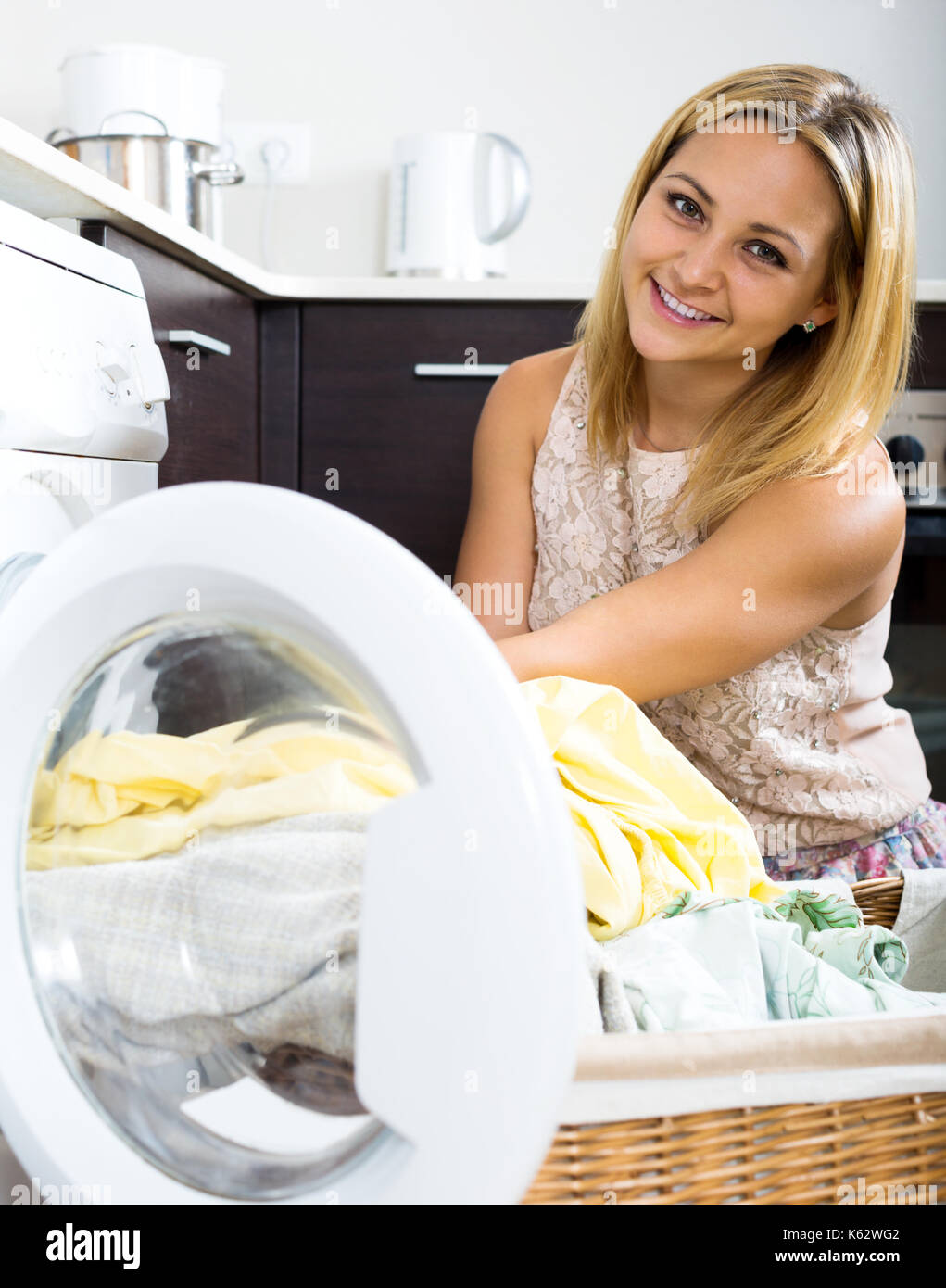 Home laundry. Blonde woman loading clothes into washing machine in home ...