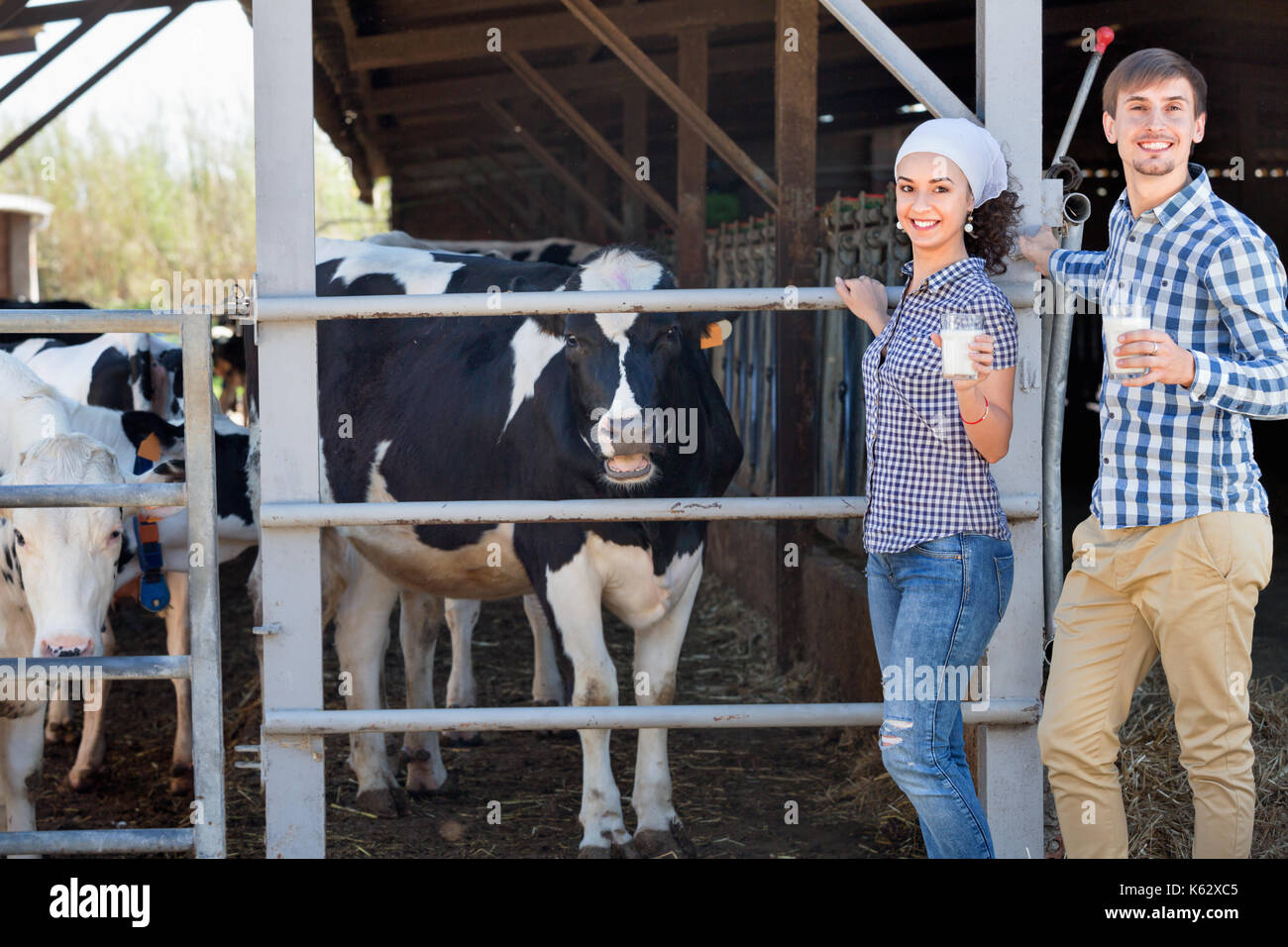 Portrait of two happy smiling farm workers holding glass with milk ...