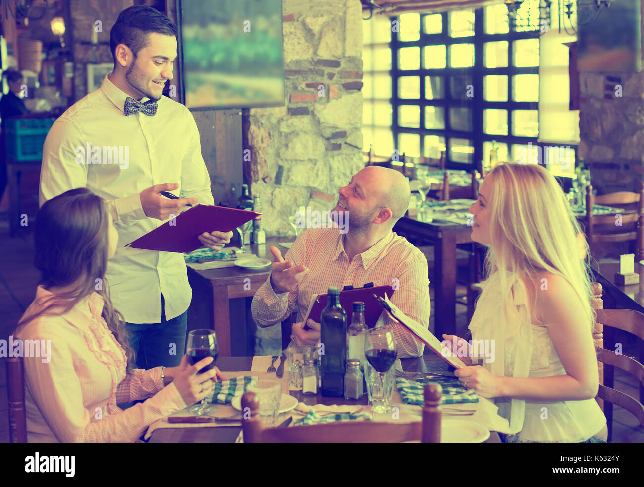 Man and two women ordering food in a restaurant. Smiling waiter is ...