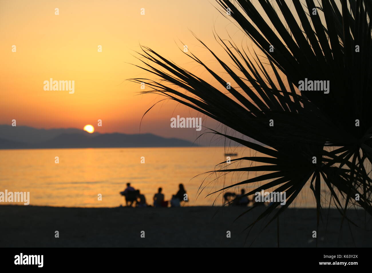 People sitting on the beach, watching the sun setting over the ...