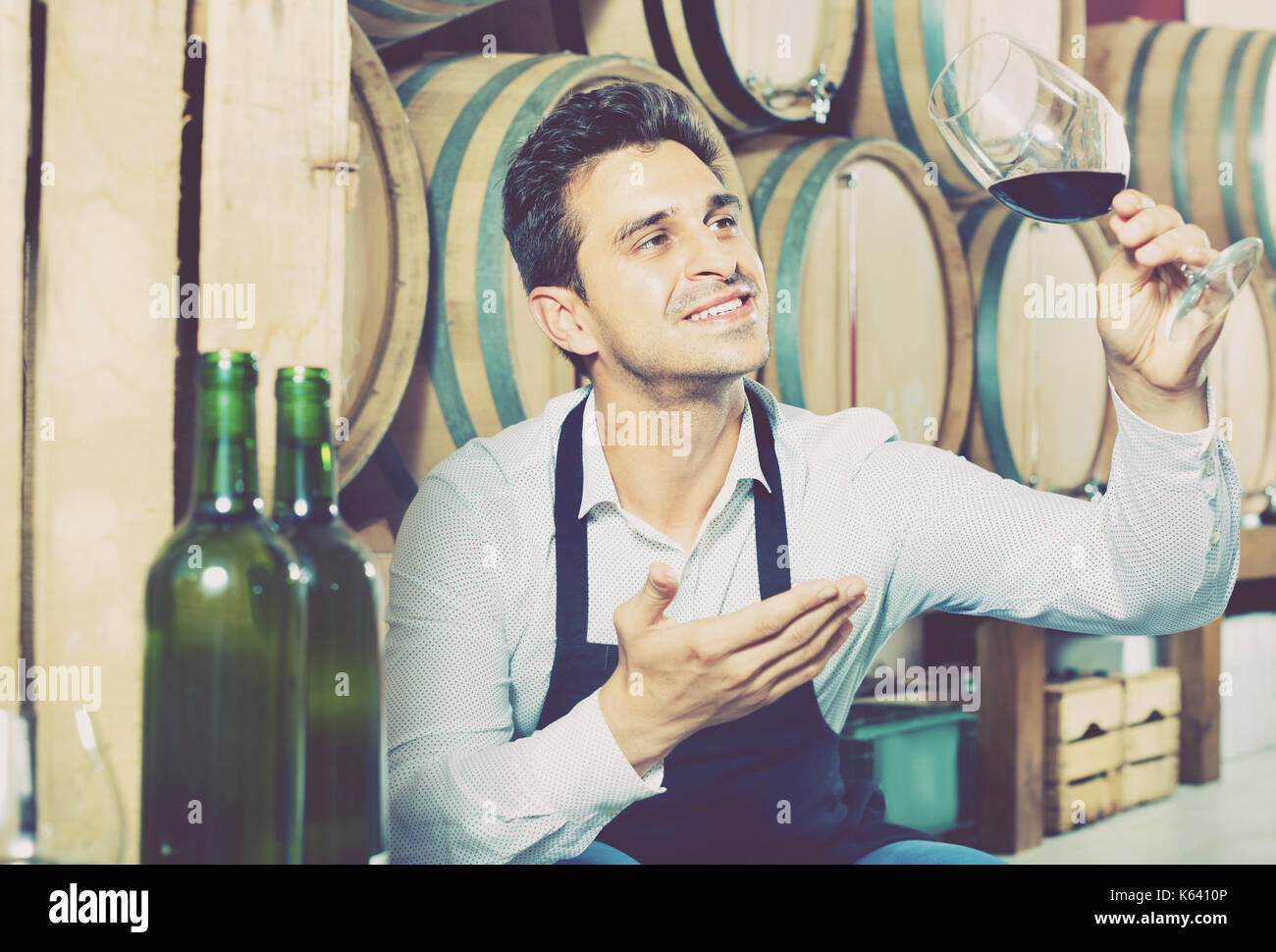 Glad man in uniform having glass with wine sample in alcohol section ...