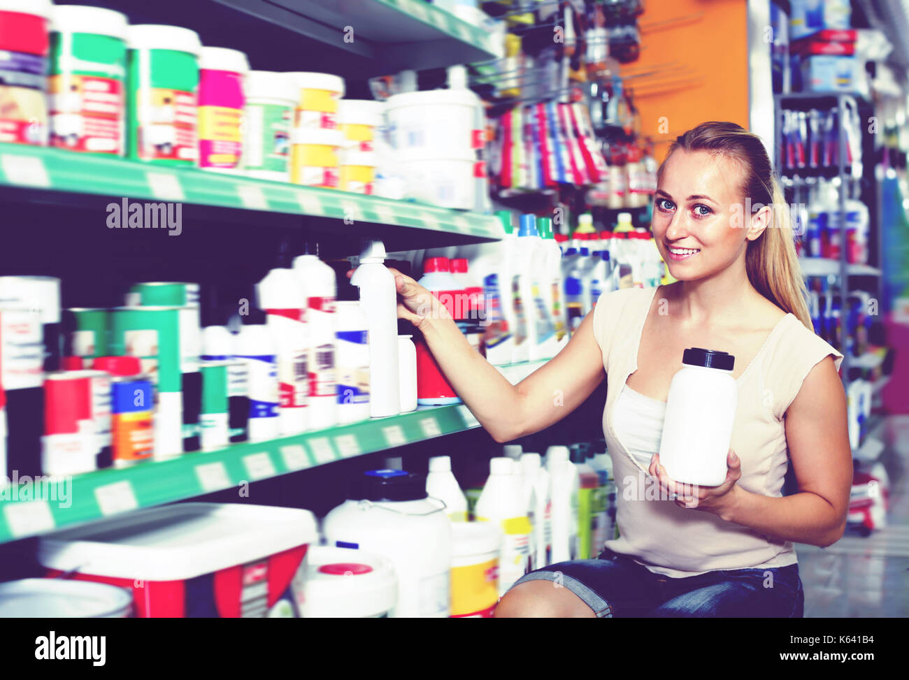 Portrait of adult female customer taking bottle with paint thinner in ...