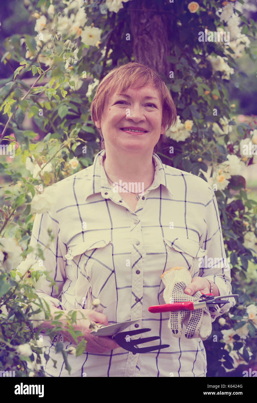 portrait of cheerful retiree woman with gardening tools standing ...