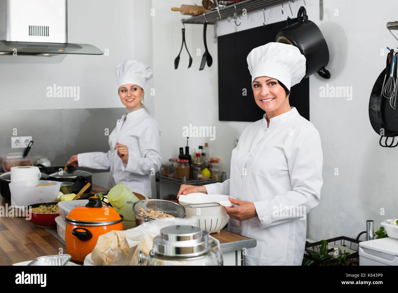 Cheerful charming female chefs preparing food on restaurant kitchen ...