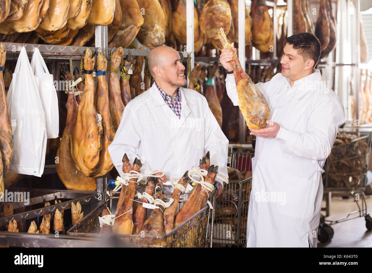 Mature butcher and his young assistant with a jamon joints at meat ...