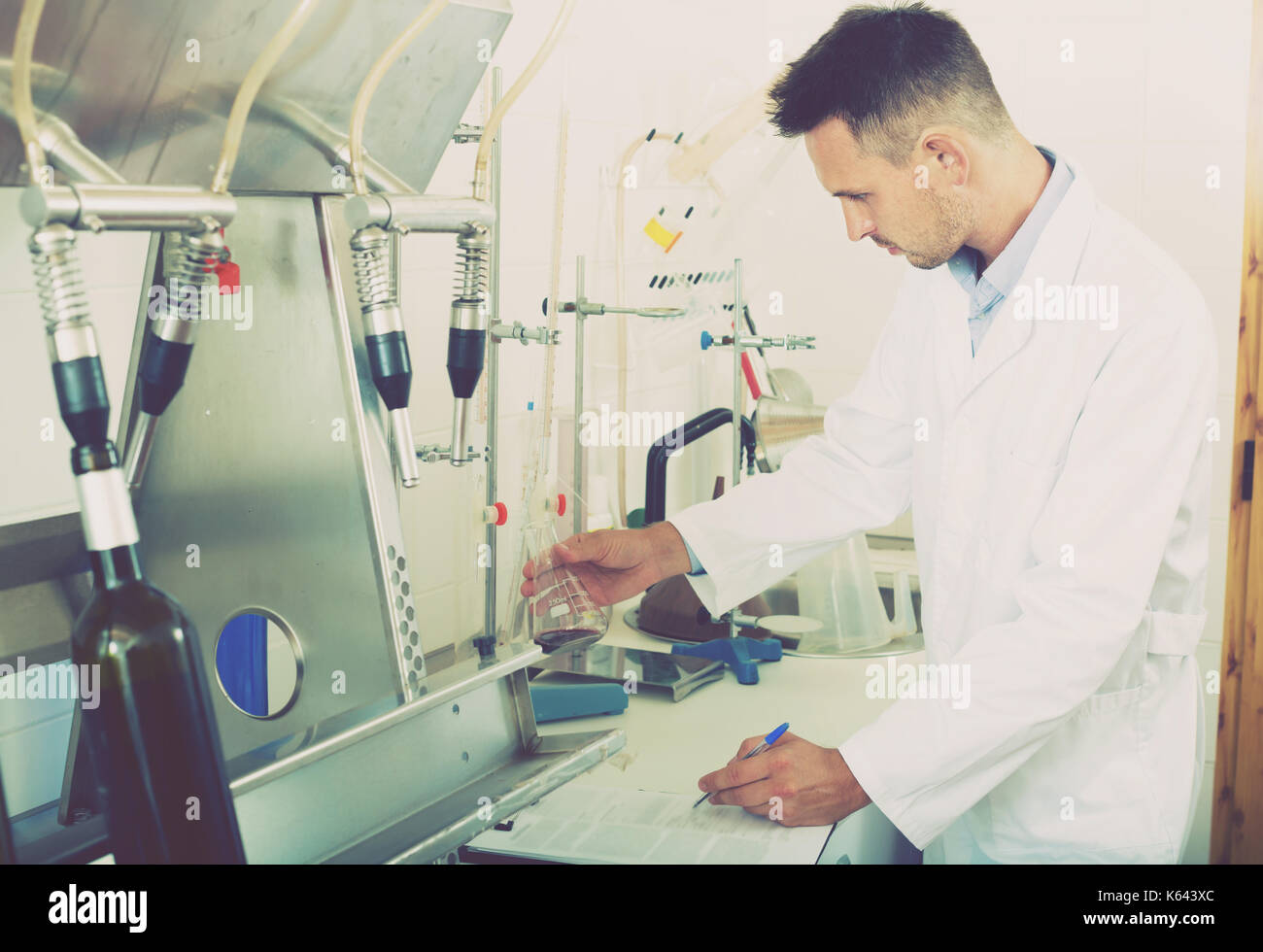 Glad man in white coat working on quality of products in winery lab ...