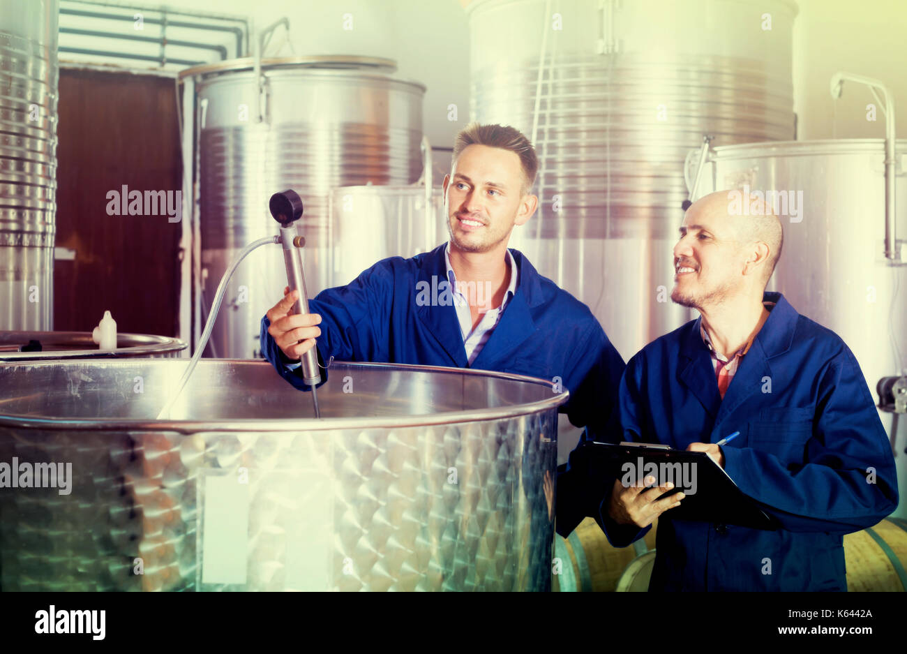 Two cheerful male winery workers in uniform working and taking notes in ...