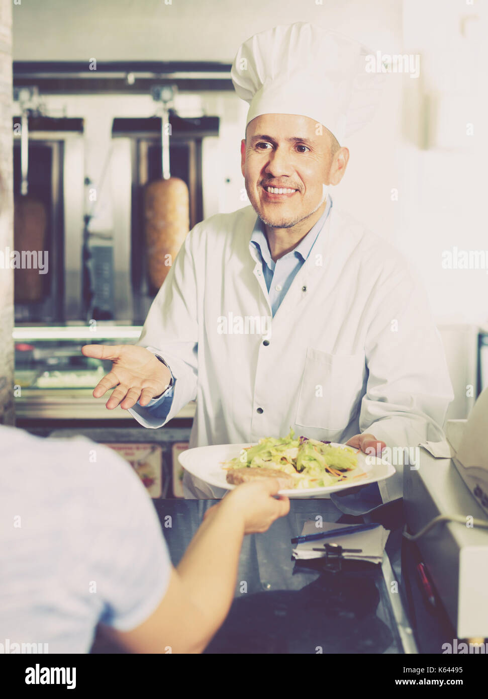 smiling man chef in uniform giving order with kebab plate to customer ...