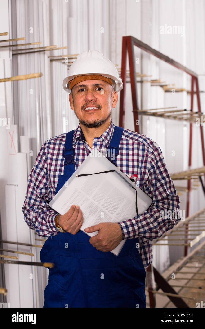Middle age workman in helmet with documents at workshop Stock Photo - Alamy