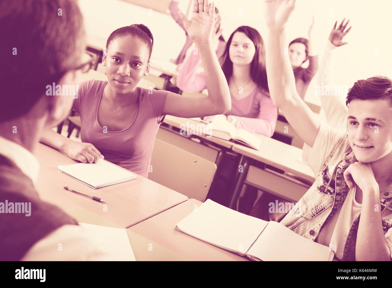 Young positive students raising their hands up to answer in the ...