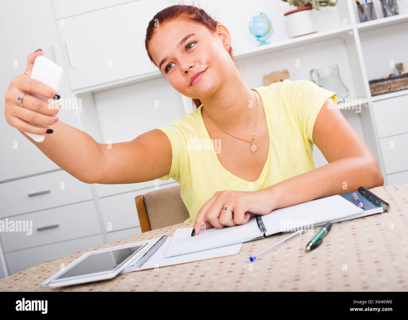ordinary teenager girl in t-shirt doing selfie during homework at the ...