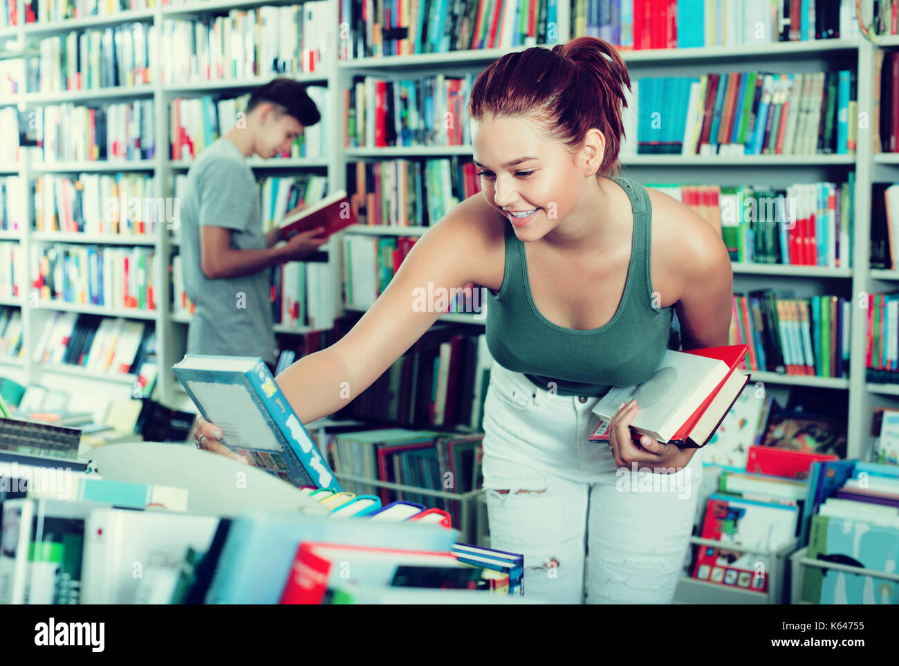 Happy teenager girl looking for new literature on shelves in book store ...
