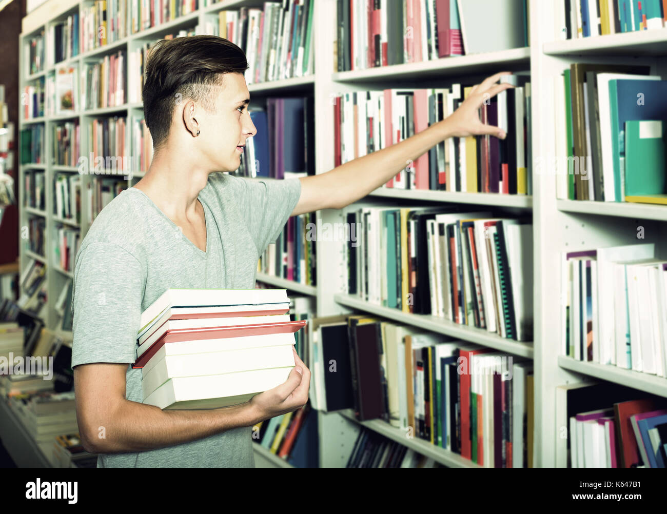 portrait of teenage smiling boy standing among bookshelves and ...