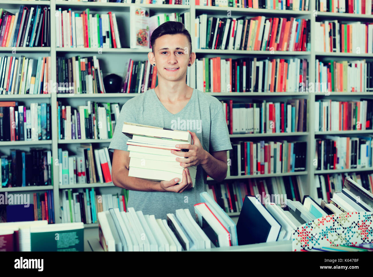 positive smiling teenage boy student holding book pile in hands in book ...