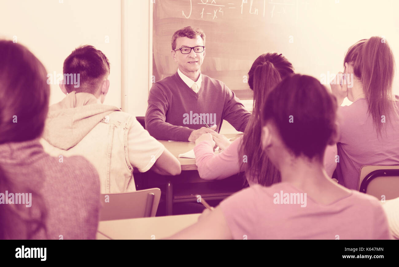 Serious elderly man giving a math lesson in front of a group of ...