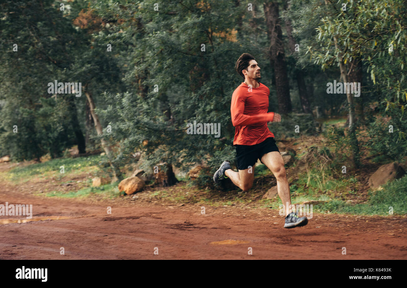 Man running on mud track. Athlete running fast in a park with dense ...