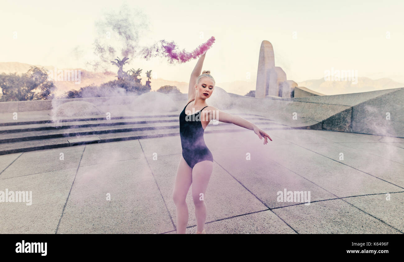 Ballet artist practicing dance moves outdoors using a pink smoke bomb ...