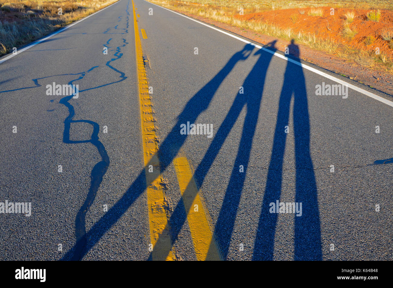 Three people cast a shadow over the road near monument valley Stock ...