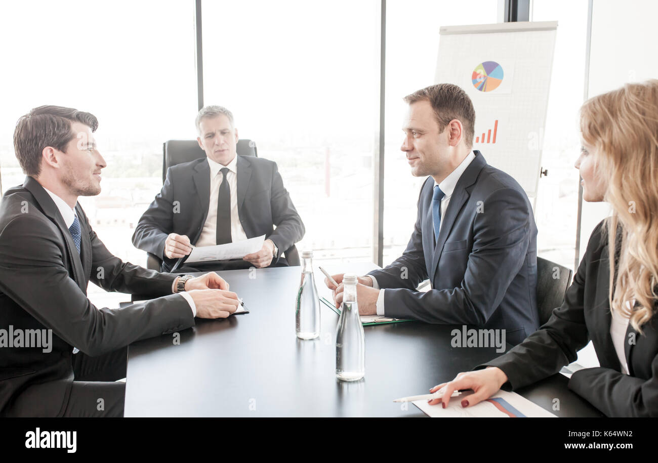 Business people sitting around meeting table, talking and working with ...