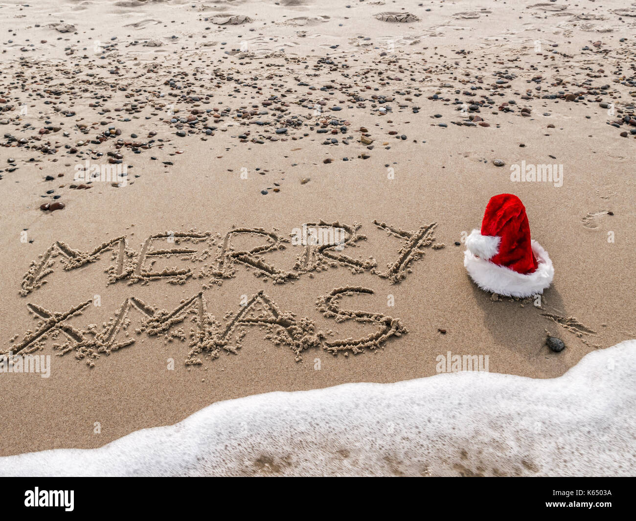 Merry Xmas greetings hand-written on the beach sand with red santa ...