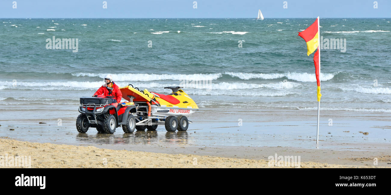 RNLI Lifeguard on the shoreline at Sandbanks beach driving a ATV quad ...