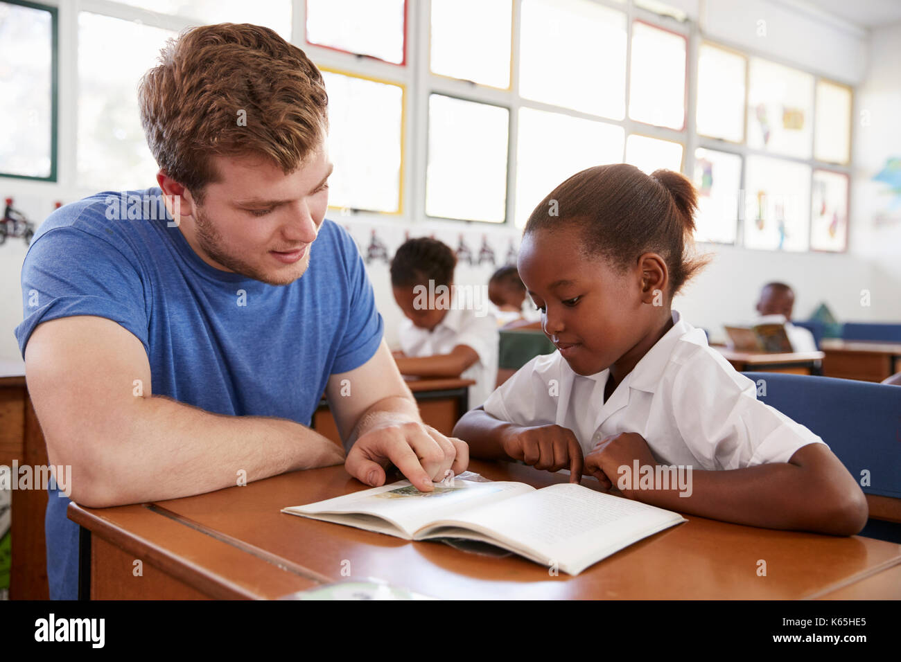 Volunteer teacher helping schoolgirl at her desk, close up Stock Photo ...