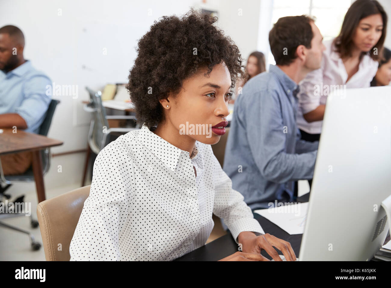 Young woman working at computer in a busy open plan office Stock Photo ...