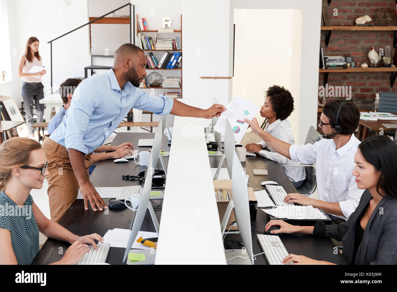 Man passing document across desk at a busy open plan office Stock Photo ...