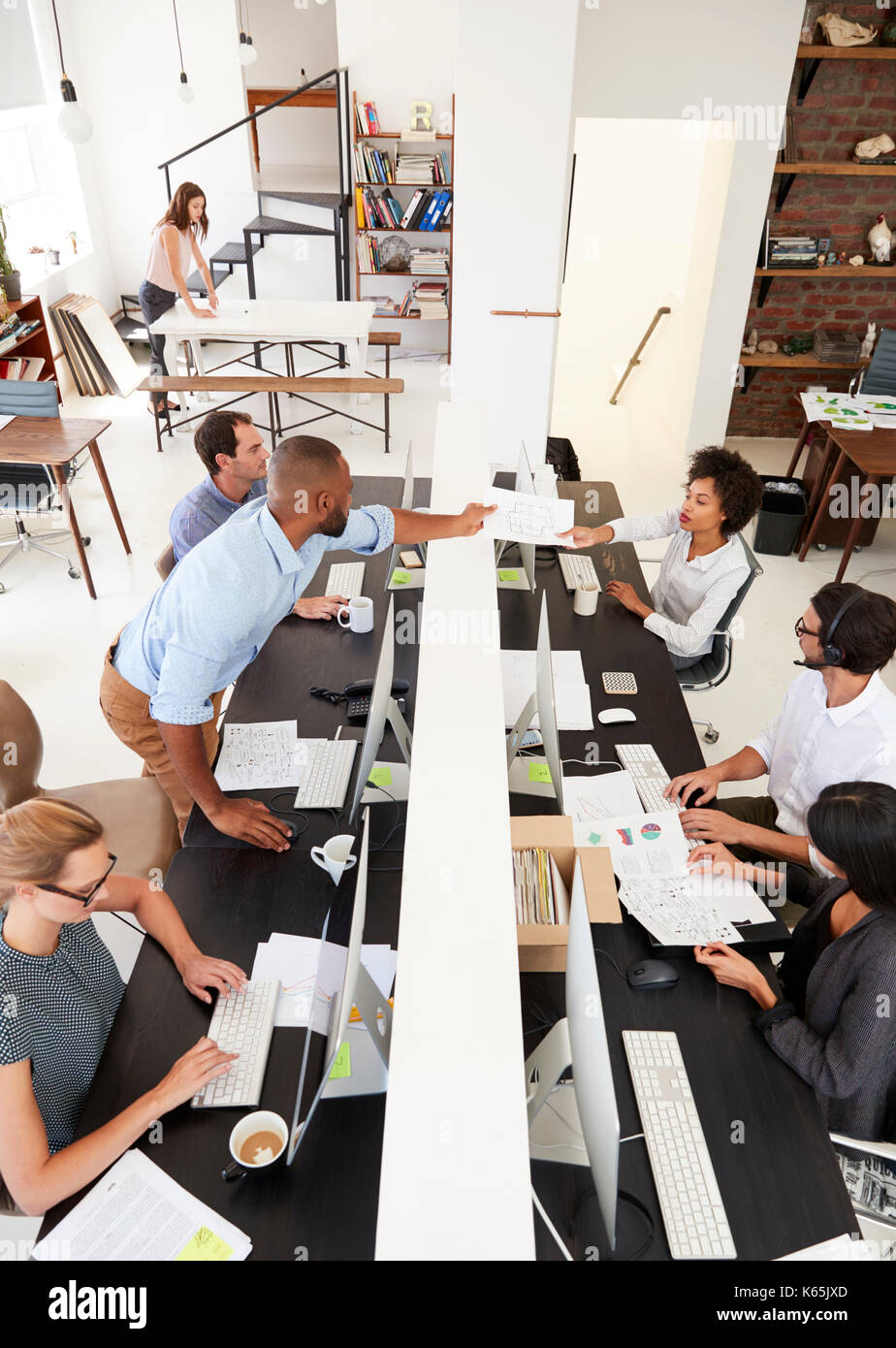 Man passing document in busy open plan office, vertical Stock Photo - Alamy