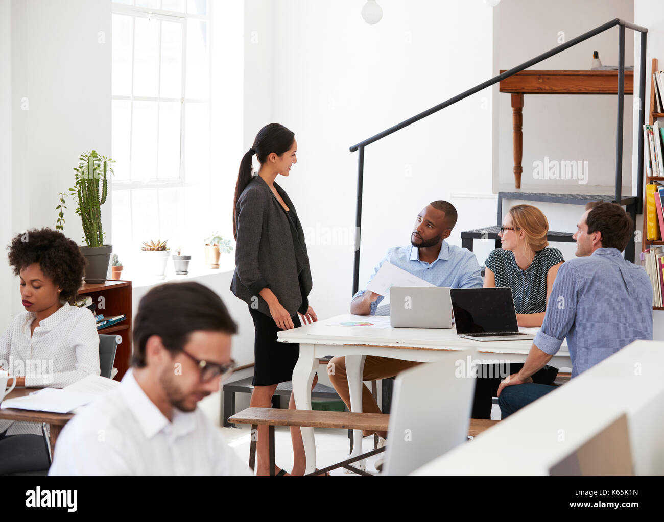 Woman talking with colleagues at a desk in open plan office Stock Photo ...