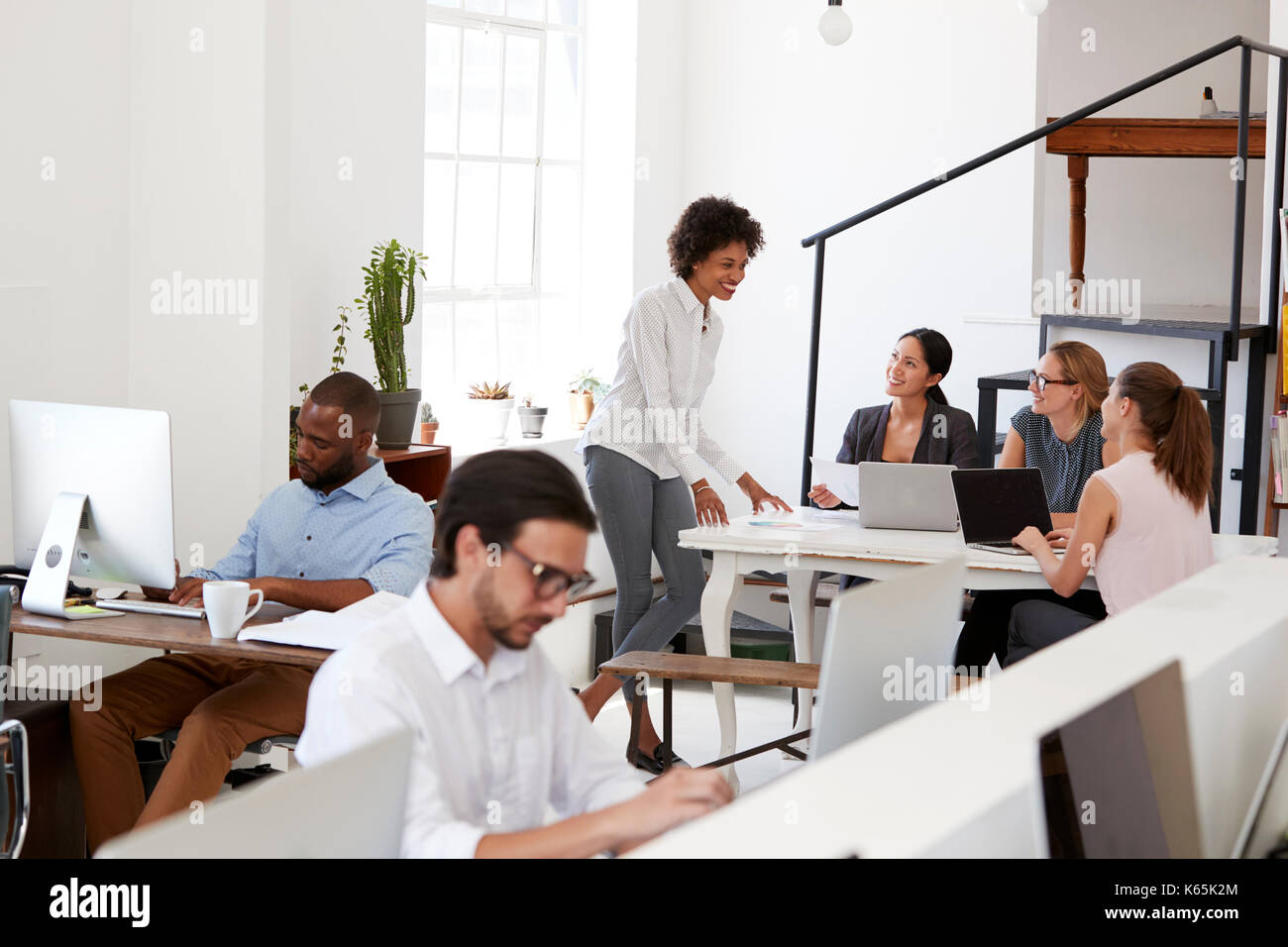 Woman briefing colleagues around a desk in open plan office Stock Photo ...