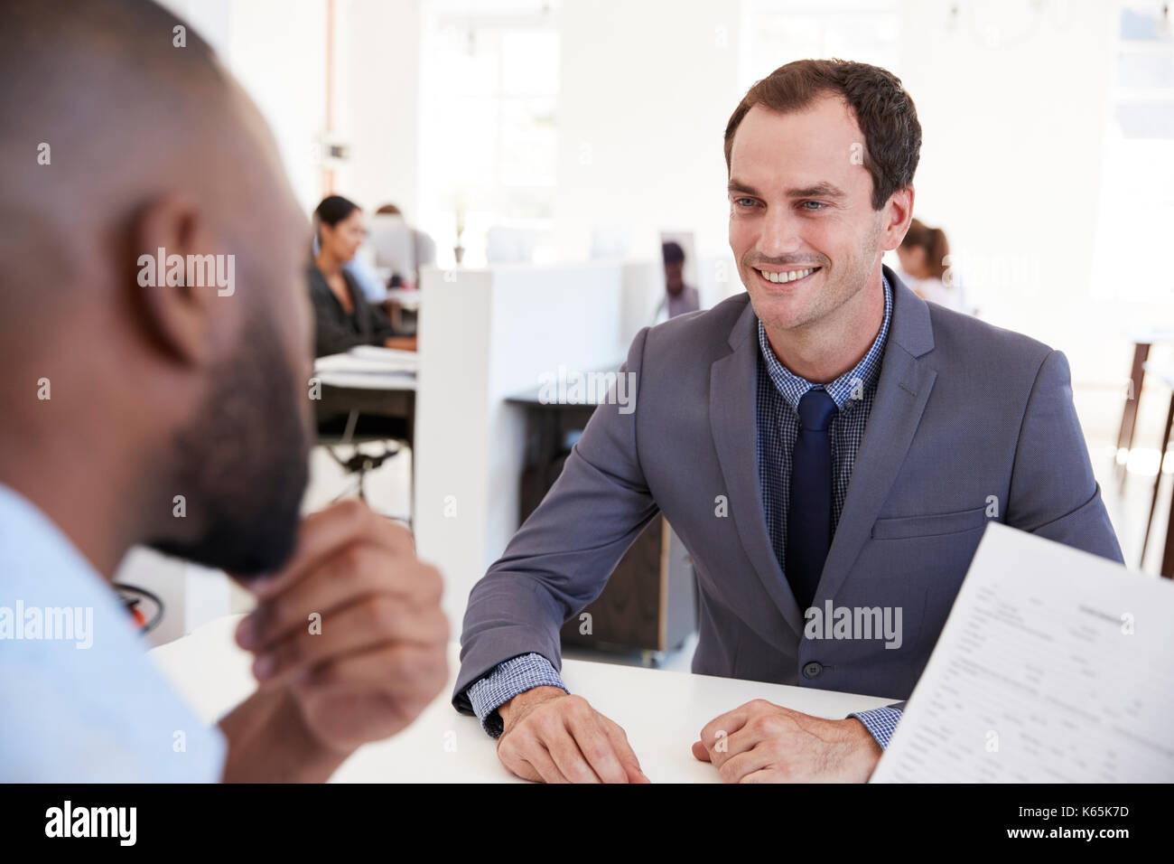 Two young men talking at a meeting in an open plan office Stock Photo ...