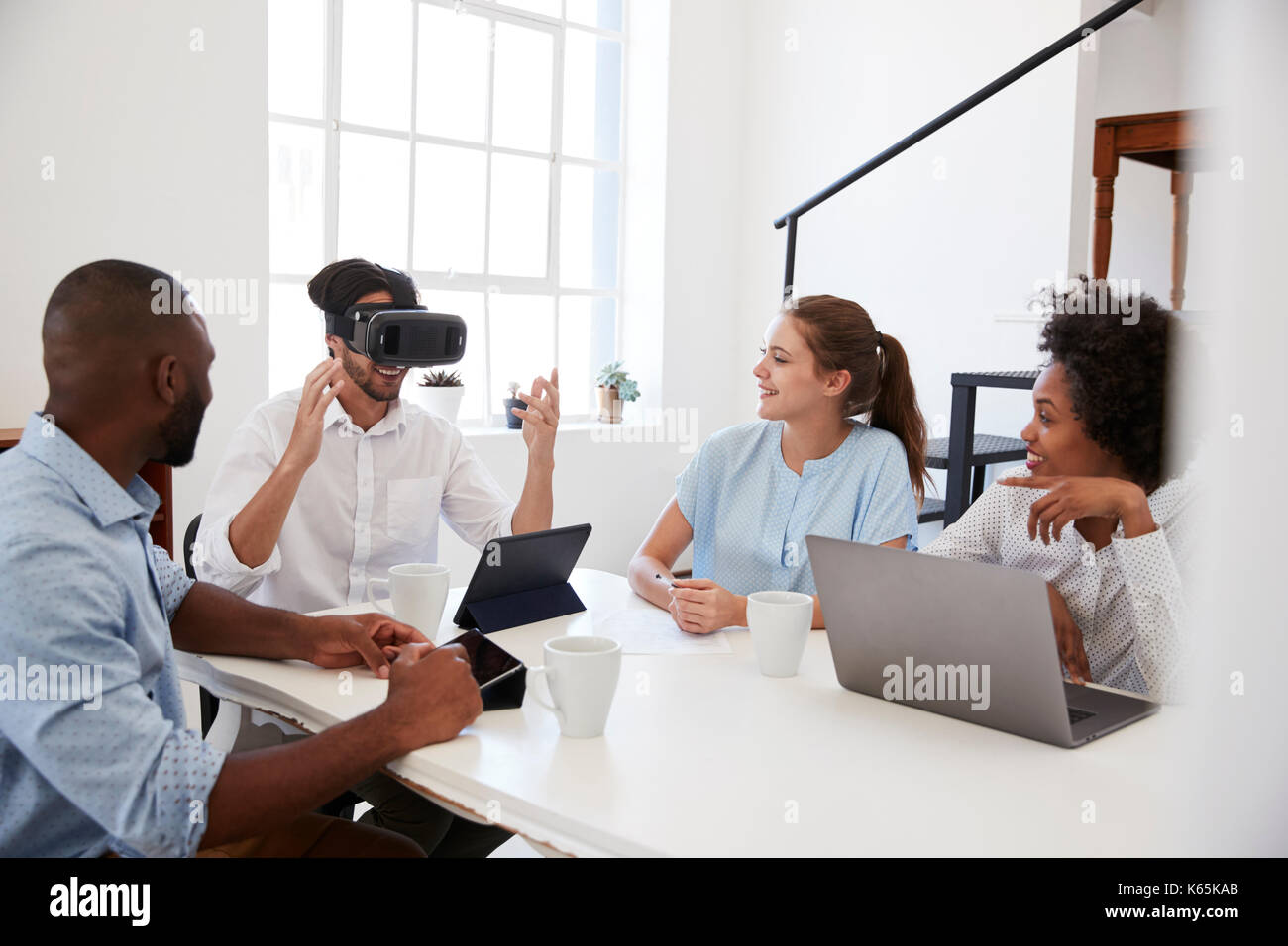 Man in VR goggles at a desk watched by colleagues in office Stock Photo ...