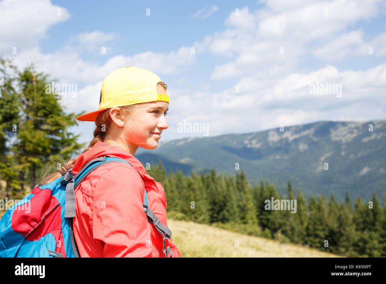 Young smiling teenage girl with backpack enjoying view in mountains ...