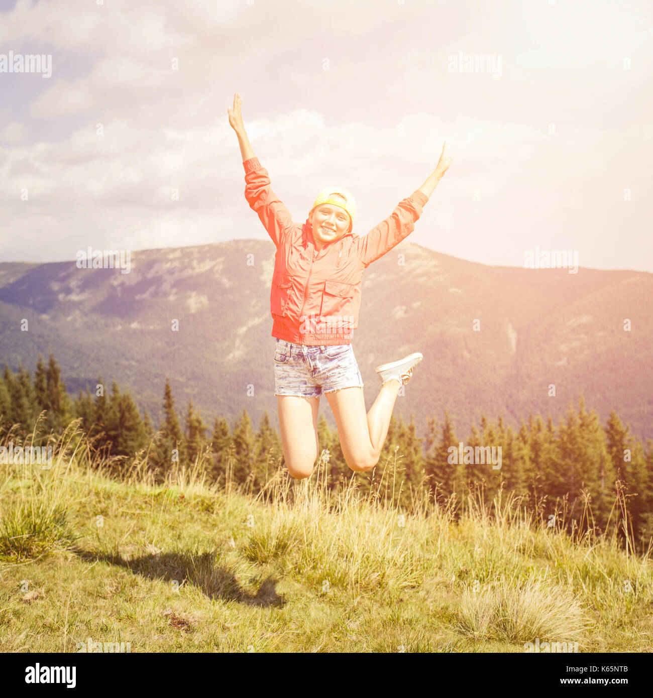 Young teenage girl jumping with raising hands over head in mountains on ...