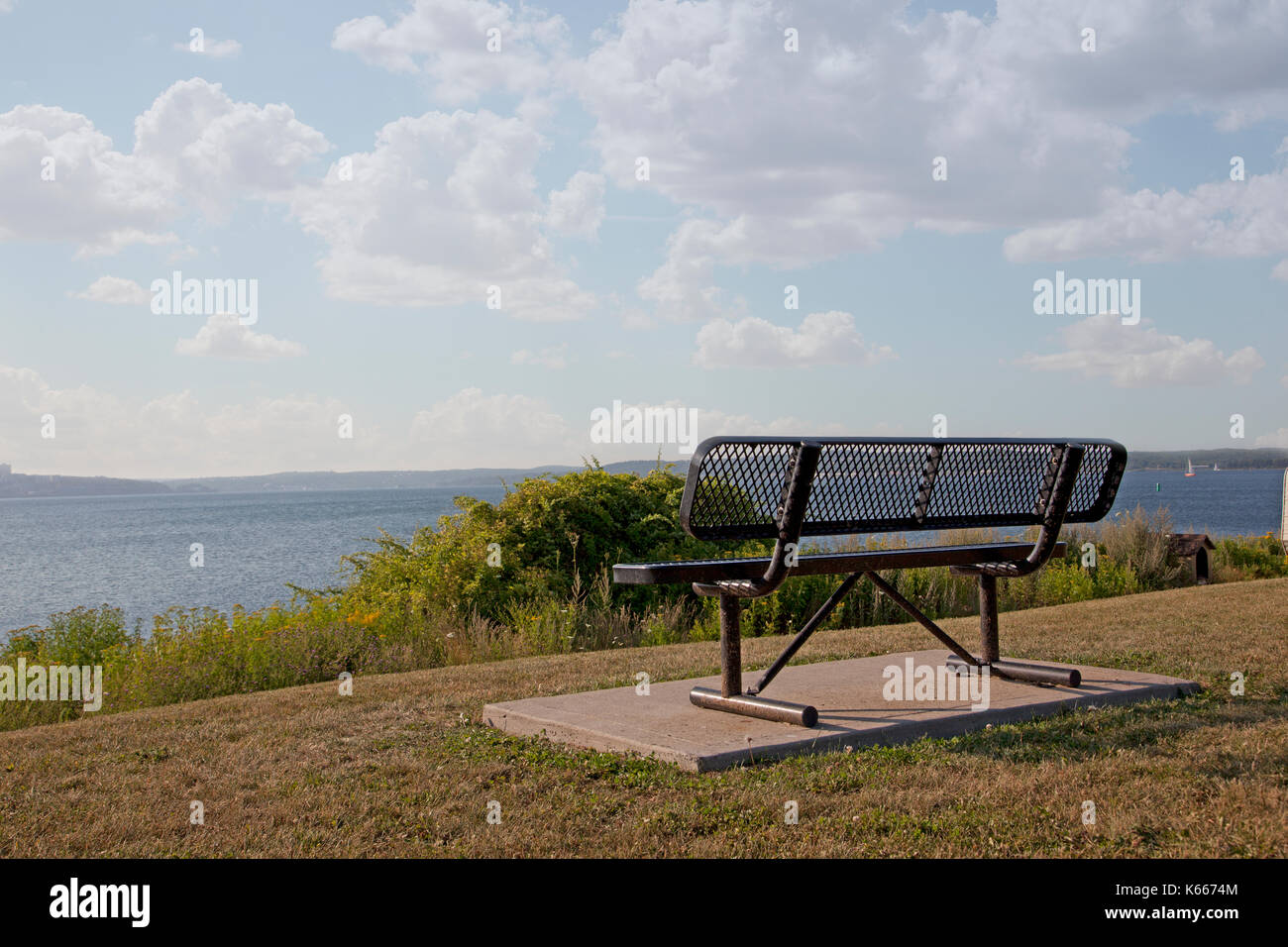 an empty metal bench in a park beside the ocean with blue sky Stock ...