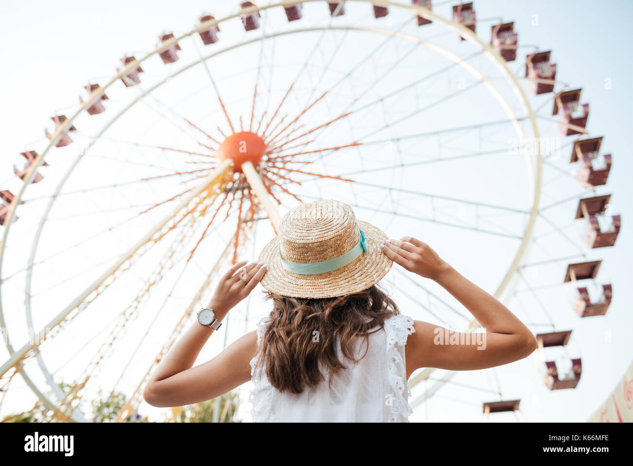 Back view of a young girl in hat standing in front of the ferris wheel ...