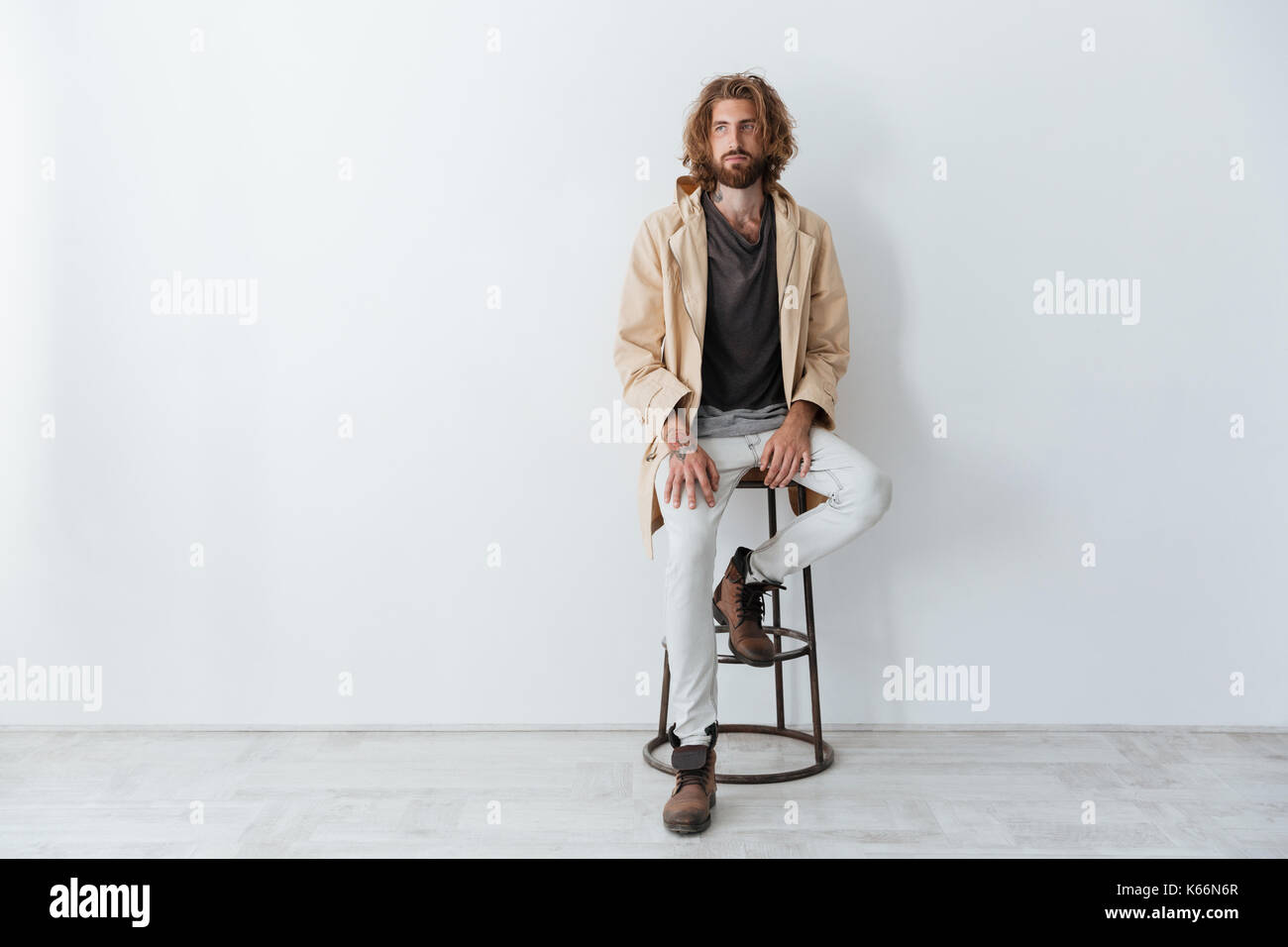 Picture of caucasian young bearded man sitting isolated over grey wall ...