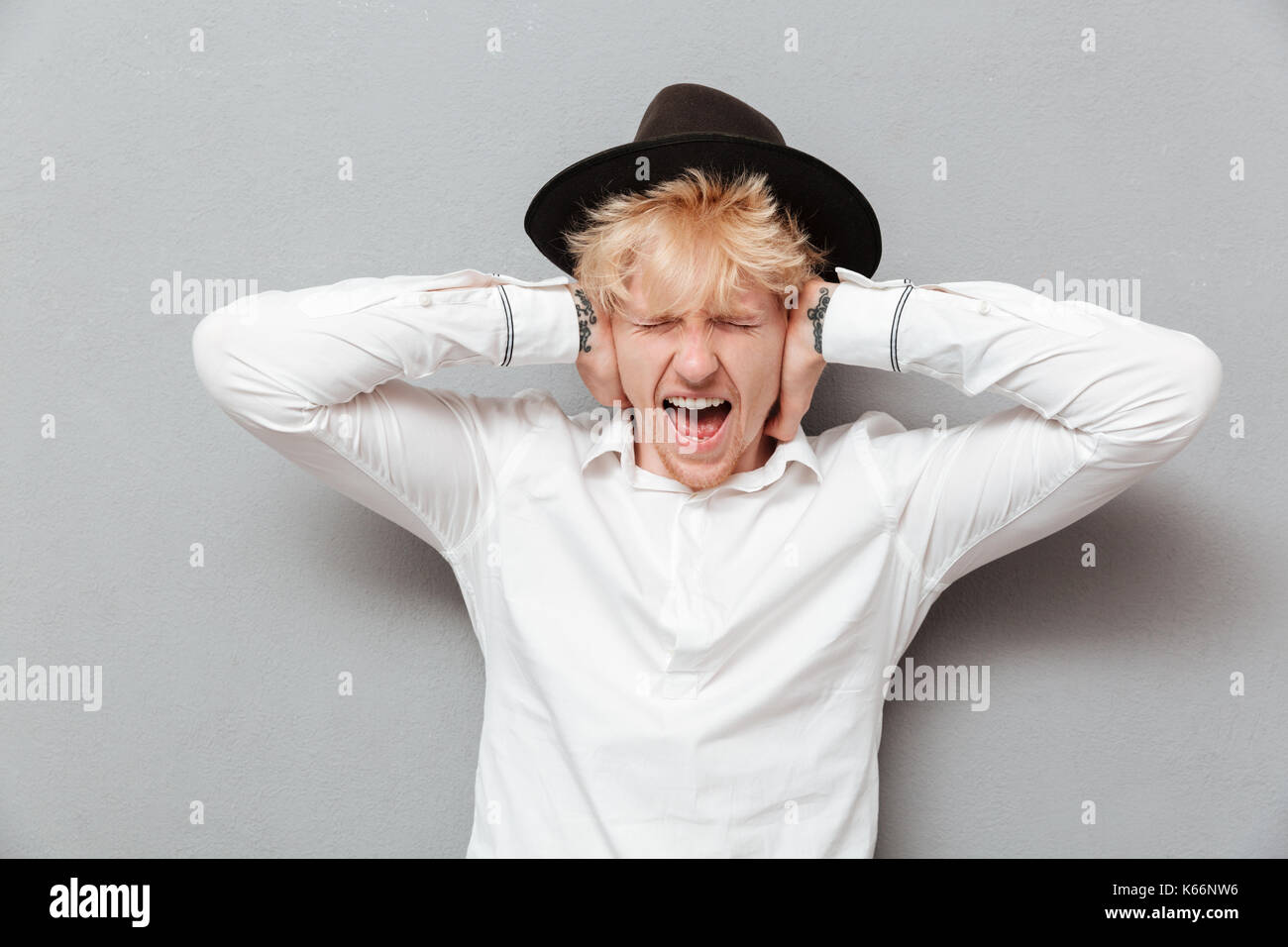 Photo of screaming young caucasian man covering ears with hands ...