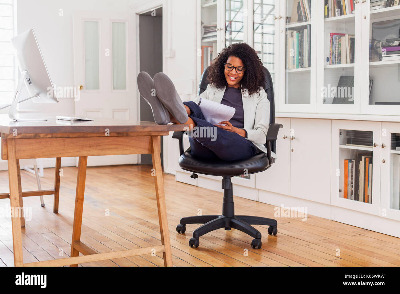Mixed Race woman with feet up writing on notepad Stock Photo - Alamy