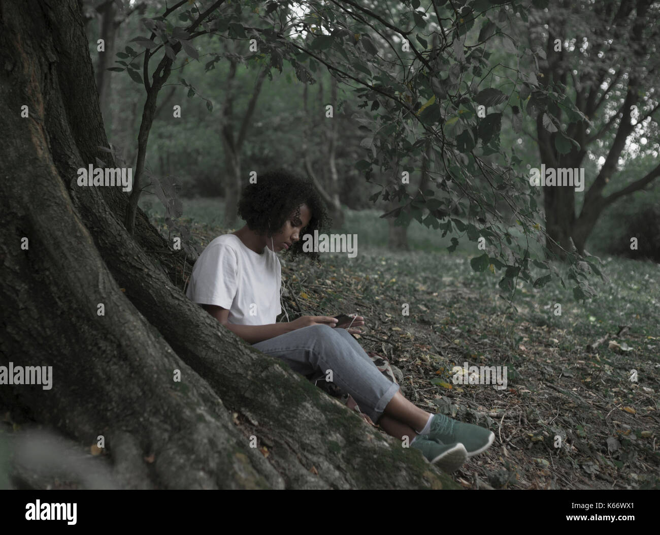 Woman sitting on tree root listening to cell phone with earbuds Stock ...