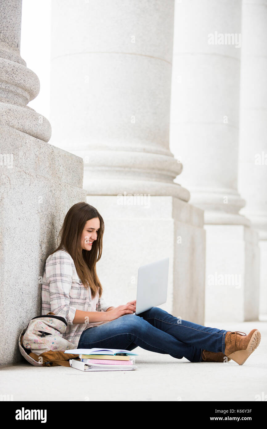 Caucasian woman leaning on pillar using laptop Stock Photo - Alamy