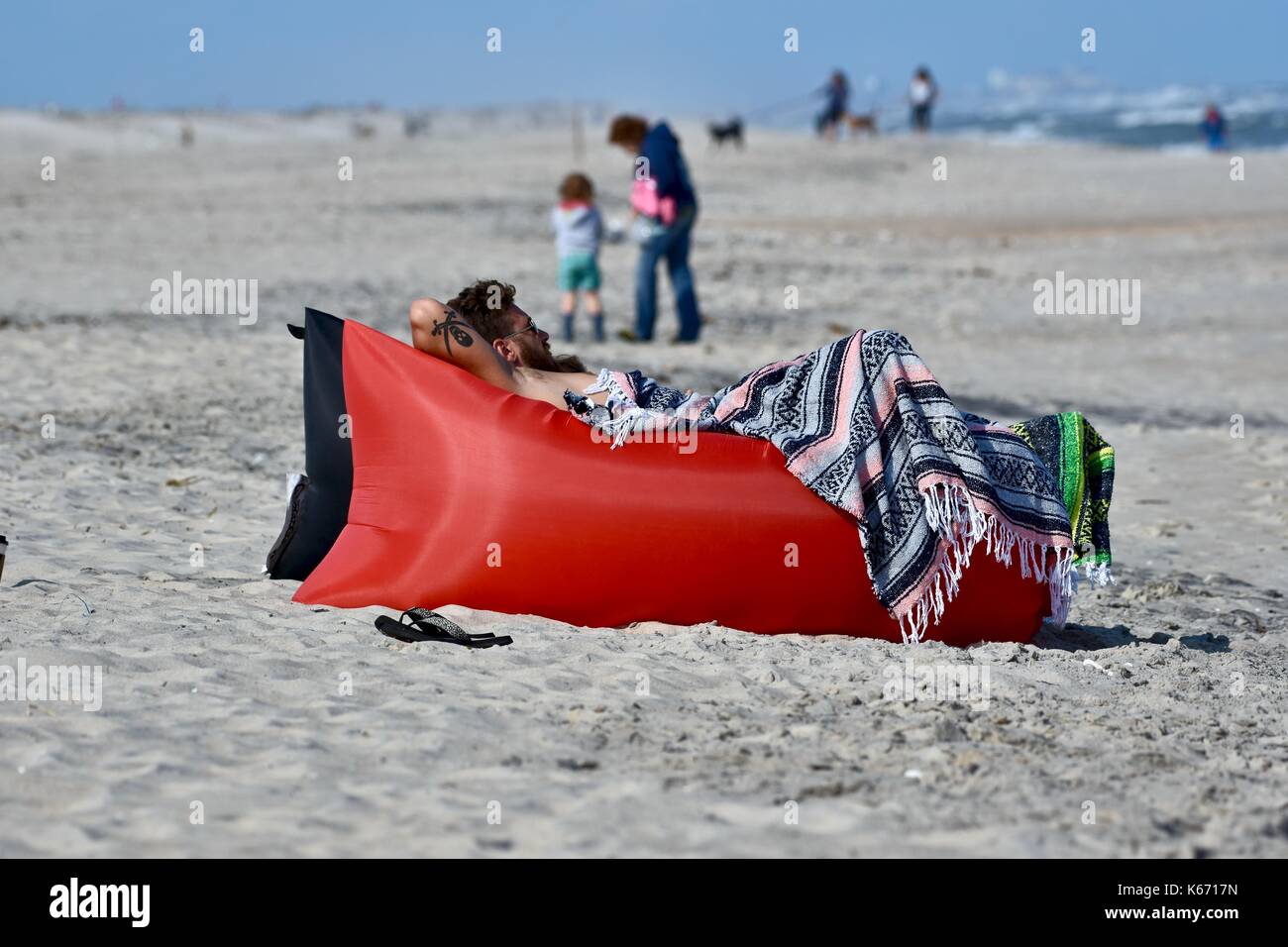 Man laying on the beach with red inflatable chair Stock Photo - Alamy