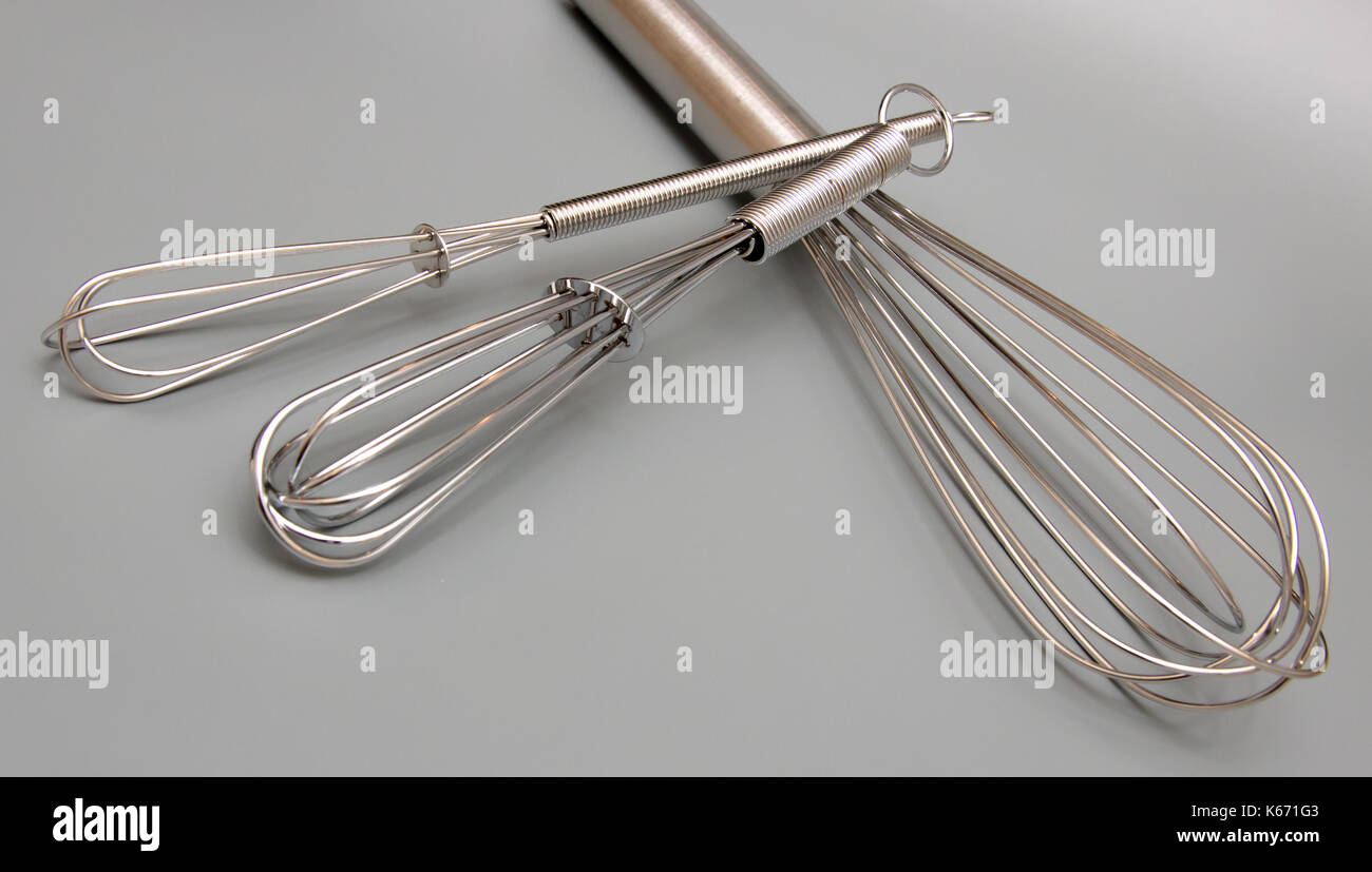 Three metal whisks on gray background Stock Photo - Alamy