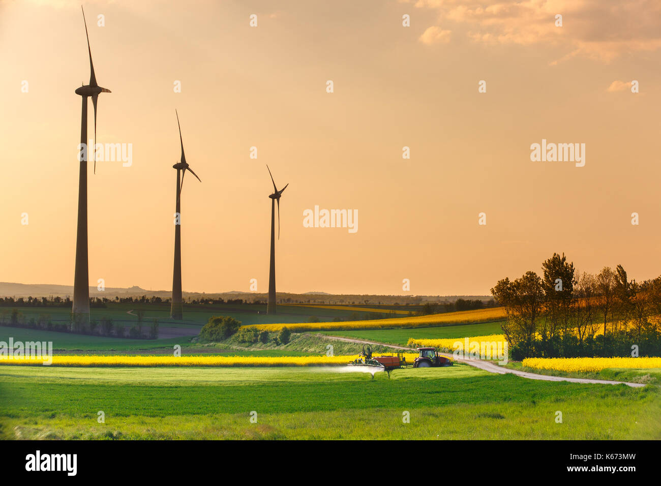 Wind farm with spinning wind turbines and tractor spraying pesticides ...