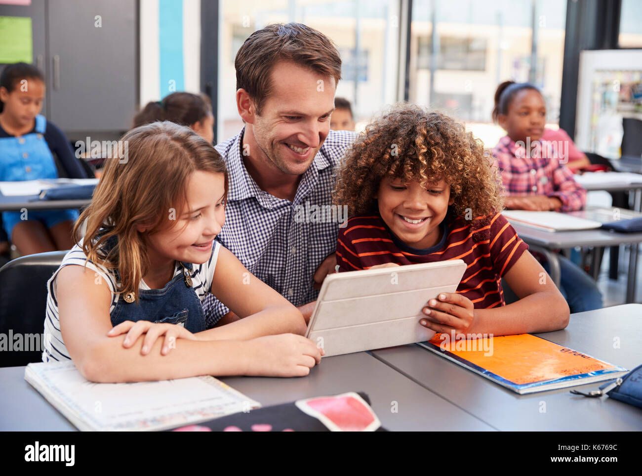 Teacher using tablet with two pupils in school class Stock Photo - Alamy