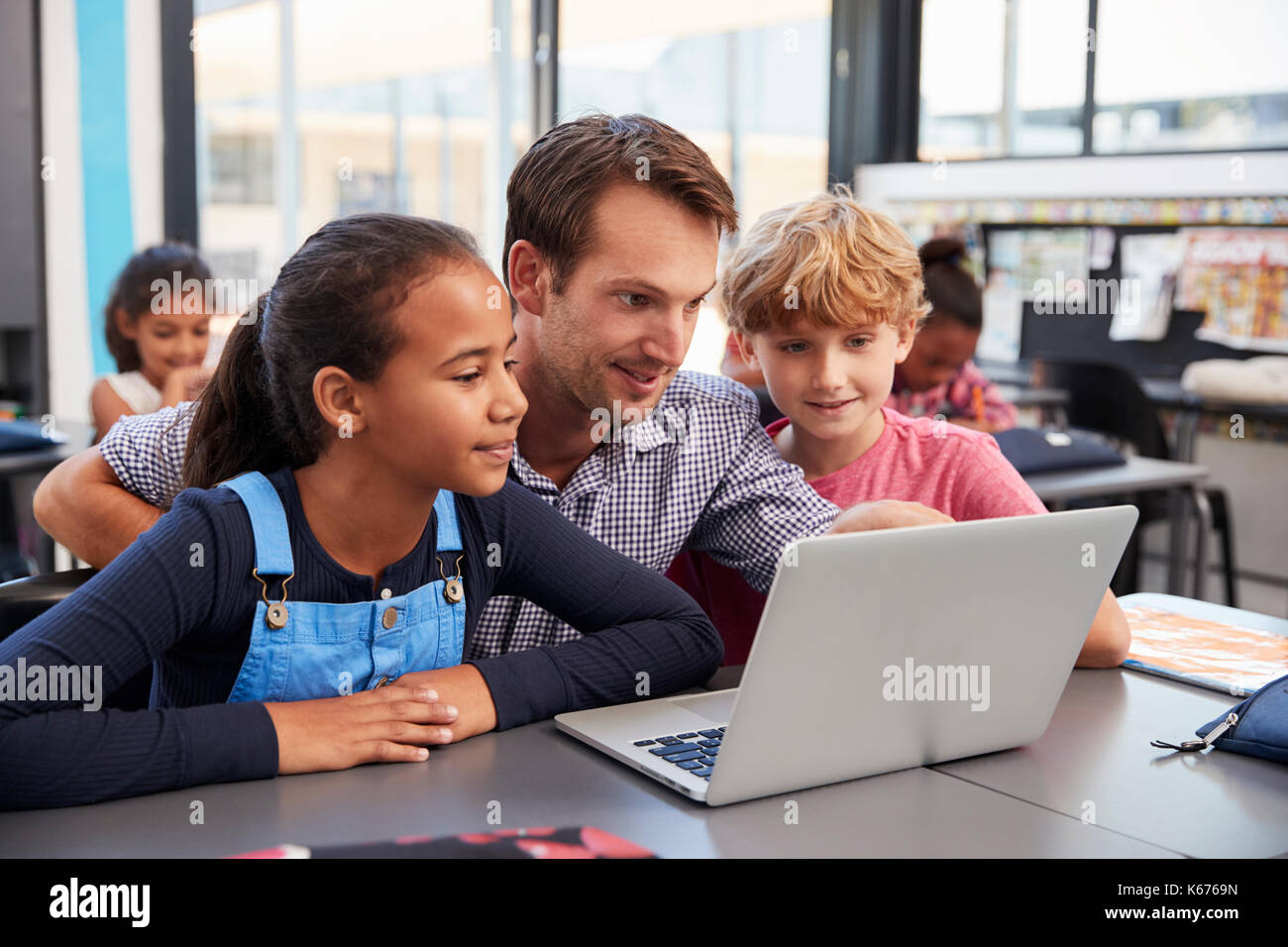 Teacher and two young students use laptop computer in class Stock Photo ...